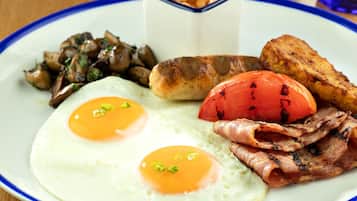 Um prato com ovos, bacon, linguiça, cogumelos, tomates assados e feijão cozido.
