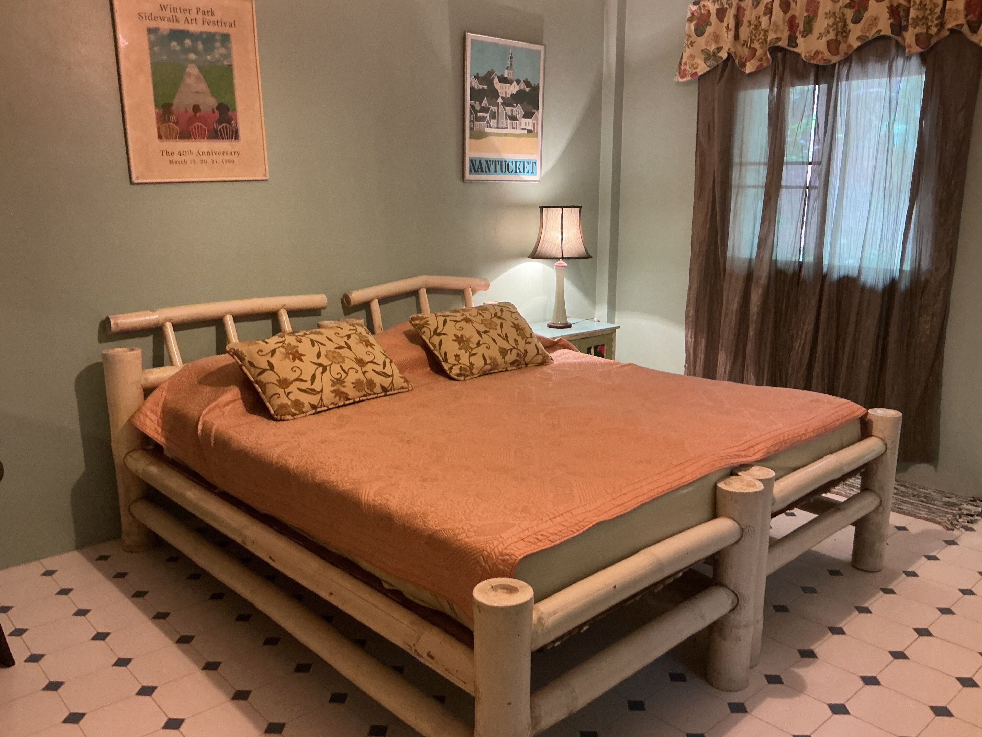 Uma cama com estrutura de madeira, duas almofadas, uma luminária e um quadro na parede.