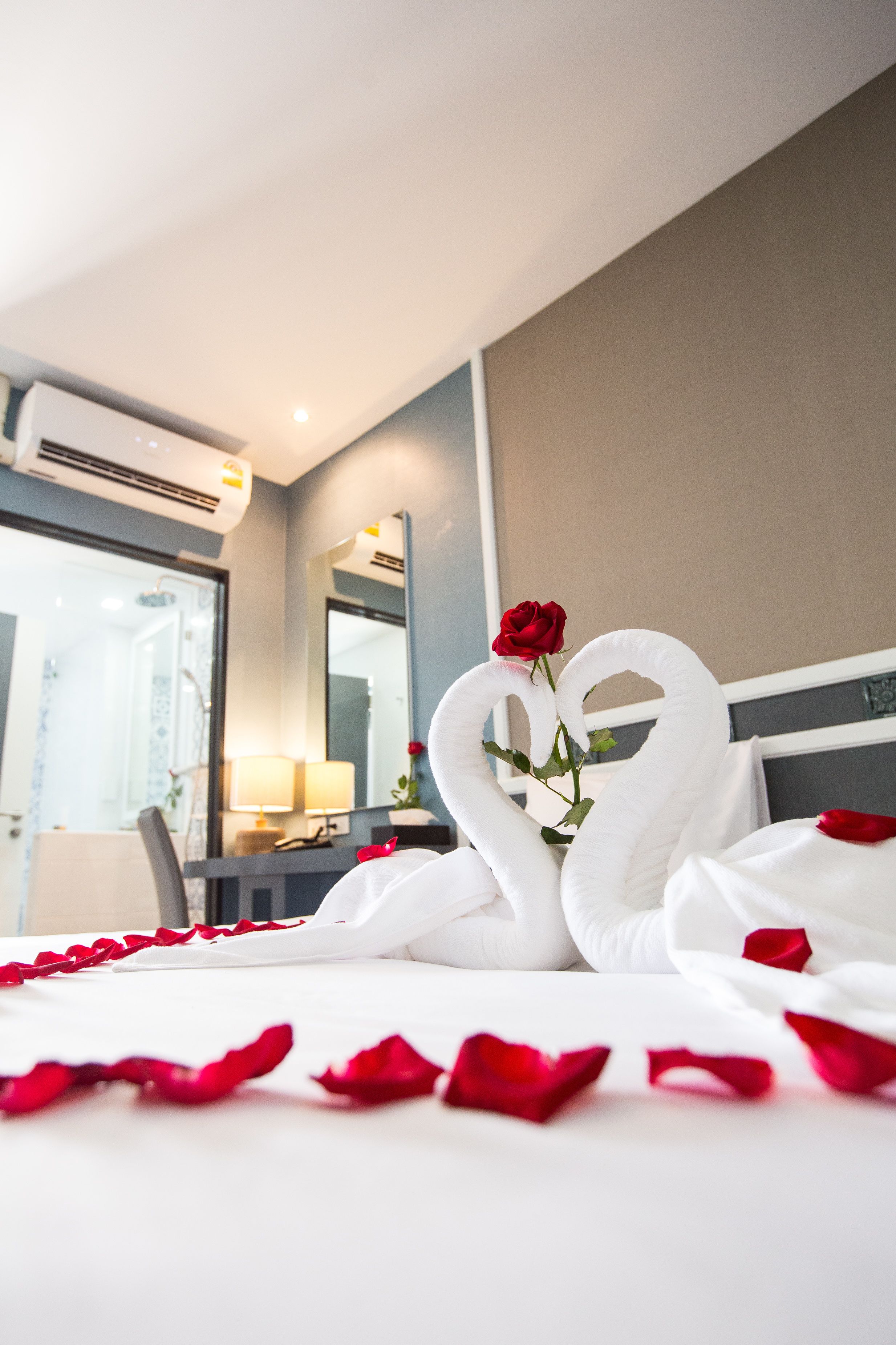 Quarto de hotel com uma cama decorada com almofadas em formato de cisne branco e pétalas de rosa vermelha.