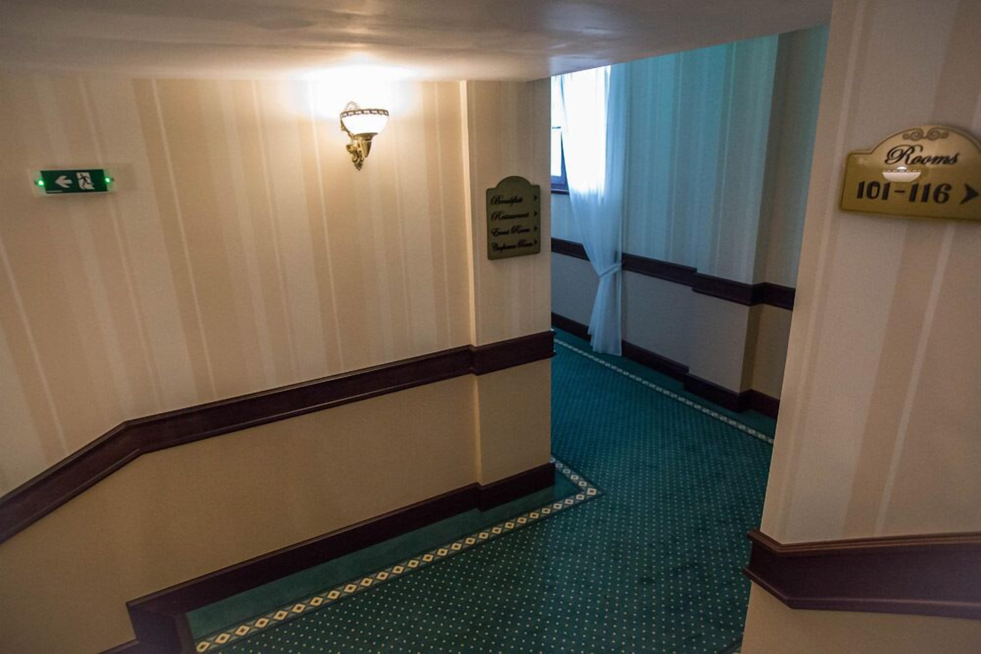 Corredor de hotel com paredes listradas, carpete com padrão verde e placas de sinalização indicando comodidades e números de quartos.