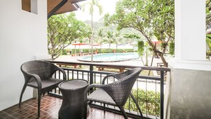 Varanda com mobiliário de vime com vista para uma área de piscina com guarda-sóis vermelhos.