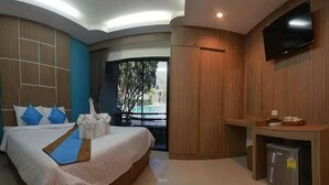Quarto de hotel com uma cama grande, televisão fixada na parede e uma pequena cozinha.