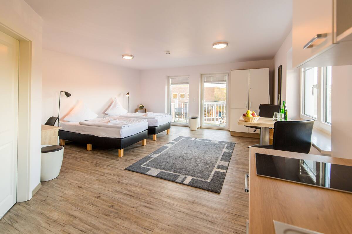 Quarto de hotel moderno com duas camas, uma escrivaninha, uma cadeira e uma varanda.