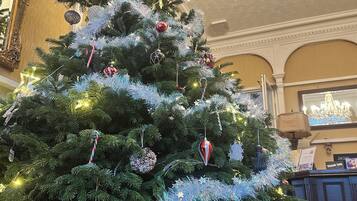 Árvore de Natal com enfeites e luzes, numa sala com um candelabro e um espelho emoldurado.