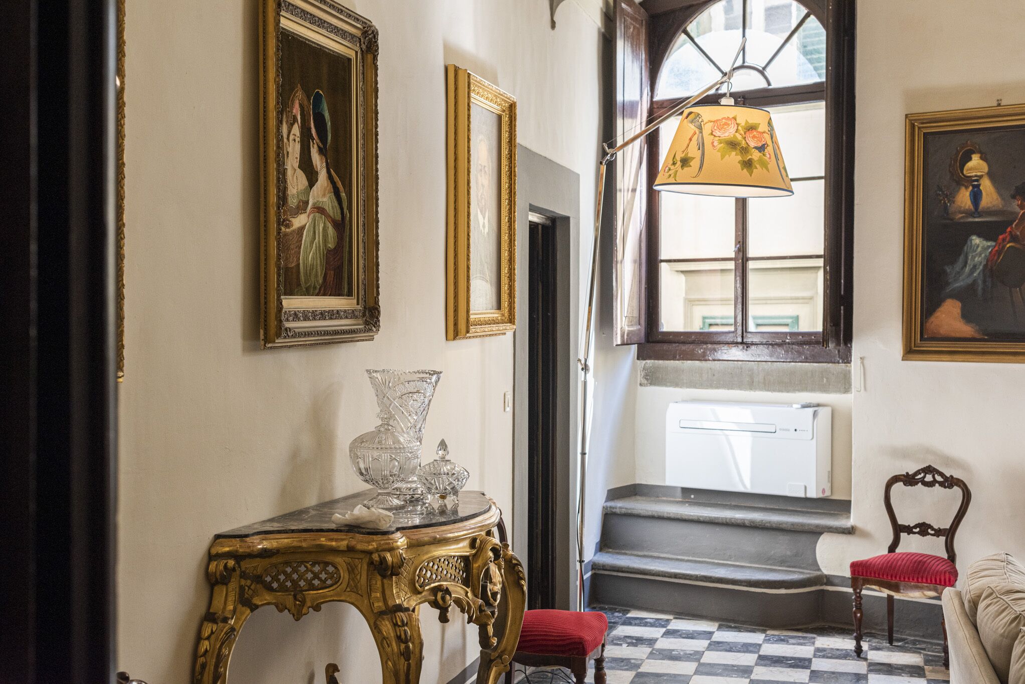 Um corredor com detalhes decorativos elaborados nas paredes, uma escadaria e um piso quadriculado.