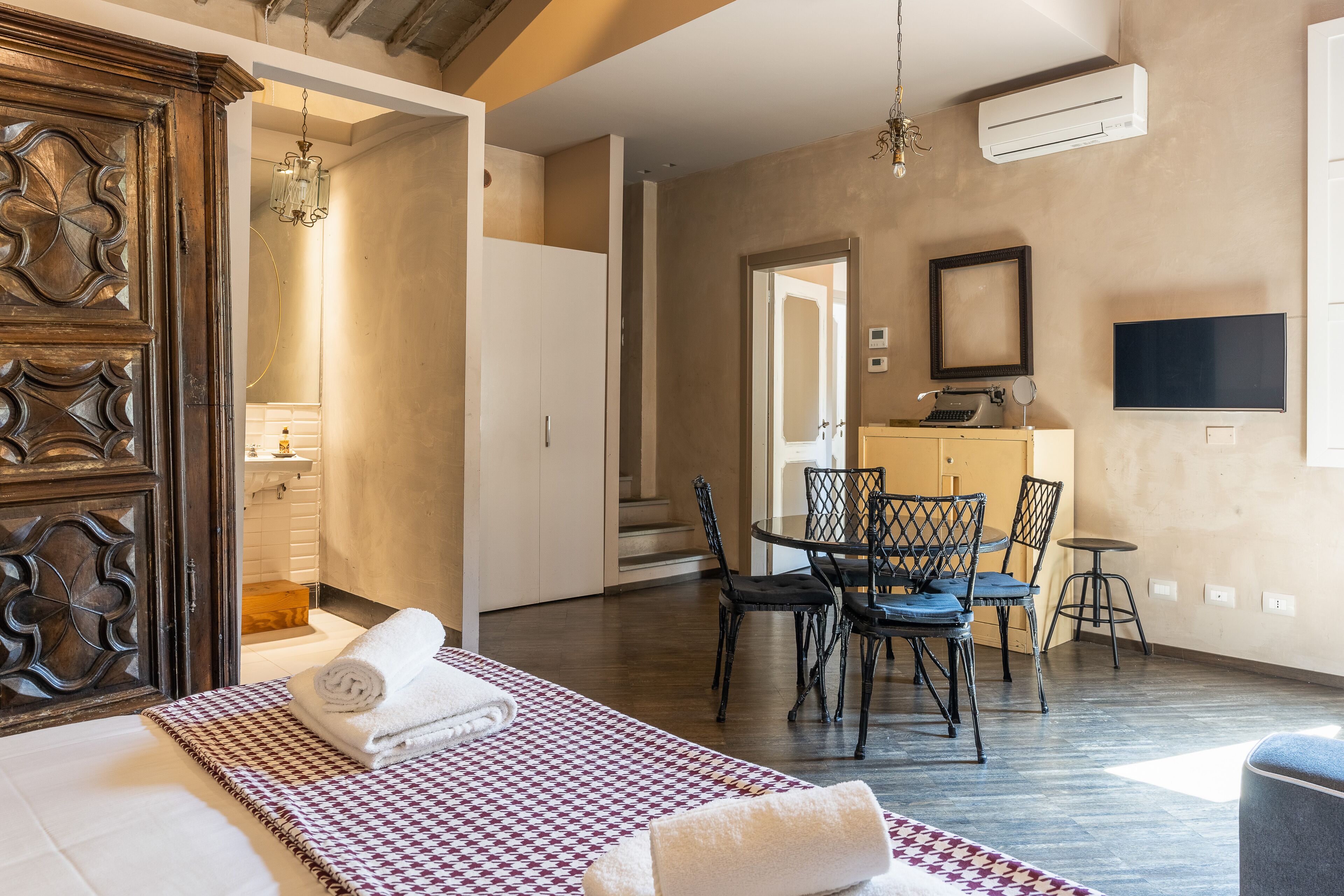 Quarto de hotel com cama, área de refeições com cadeiras, televisão e aparelho de ar condicionado.