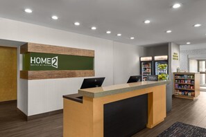 Balcão de recepção de hotel com uma placa indicando 'HOME 2 SUITES BY HILTON' e um monitor de computador.