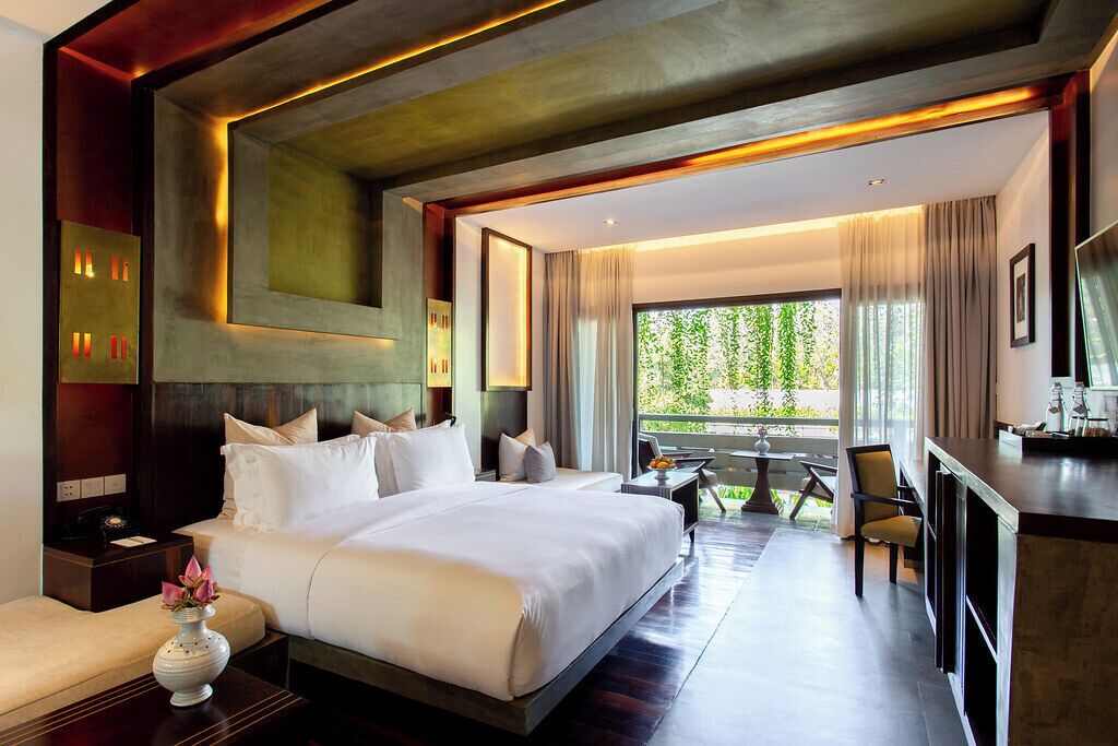 Quarto de hotel moderno com uma cama grande, uma escrivaninha e vista para o verde lá fora.