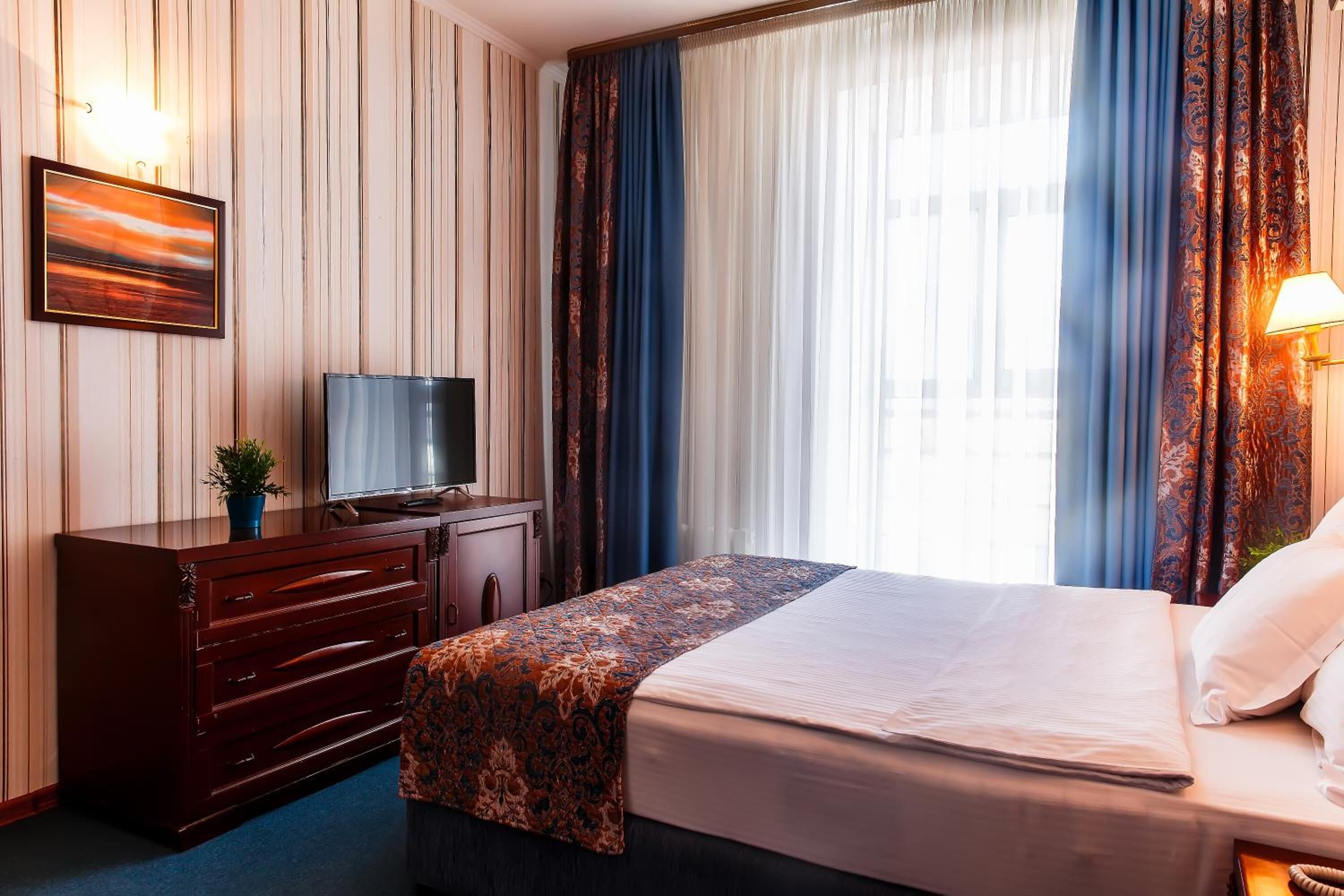 Quarto de hotel com cama, televisão, penteadeira e janela com cortinas.