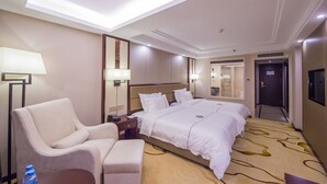 Quarto de hotel com uma cama grande, uma cadeira, uma escrivaninha e um abajur.