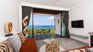 Uma sala de estar moderna com uma grande porta de vidro que dá para uma varanda com vista para o oceano.