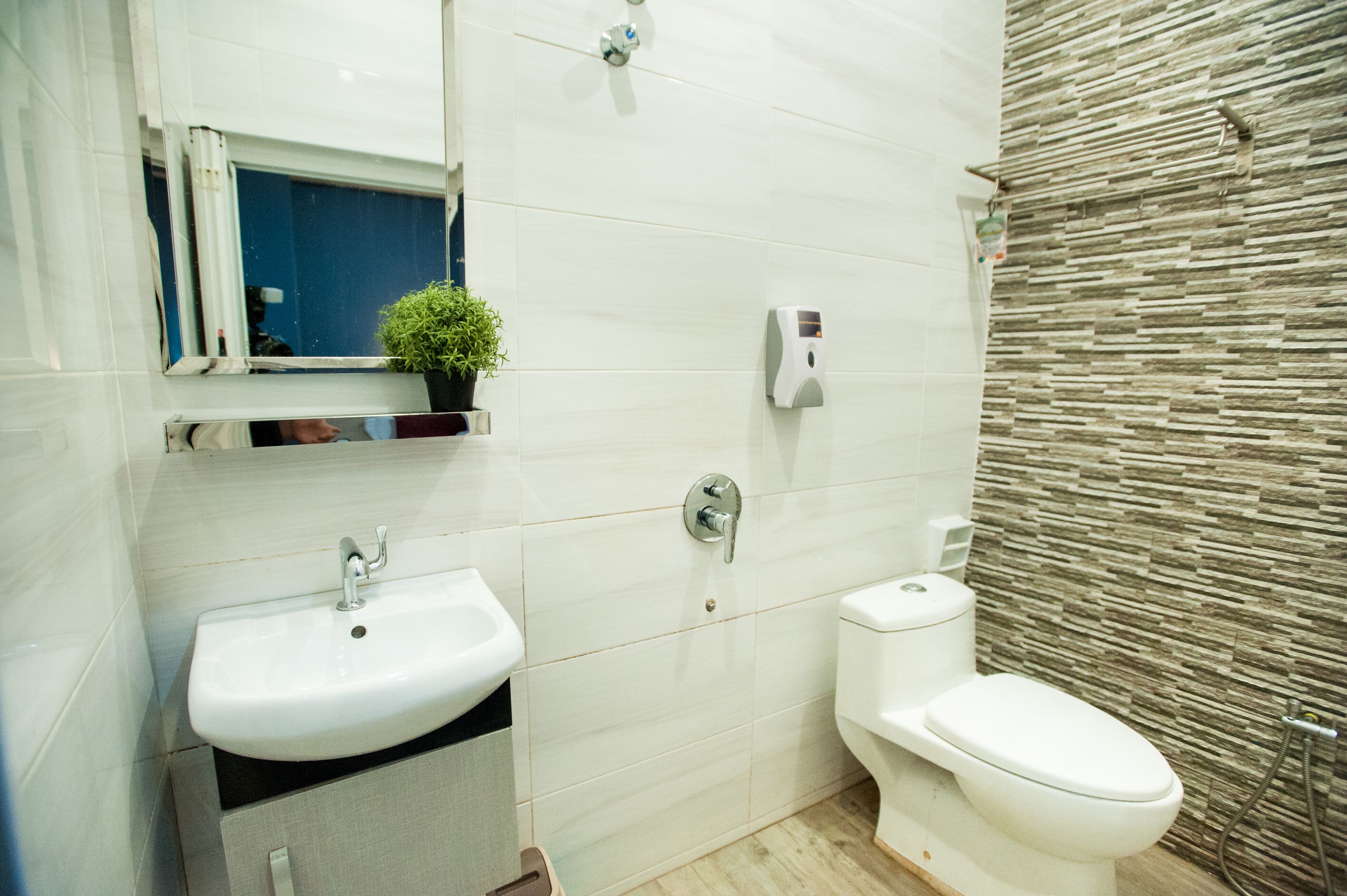 Uma casa de banho moderna com lavatório branco, sanita e parede com textura de pedra.