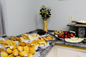 Mesa de buffet com diversos alimentos, incluindo pães, doces e frutas.
