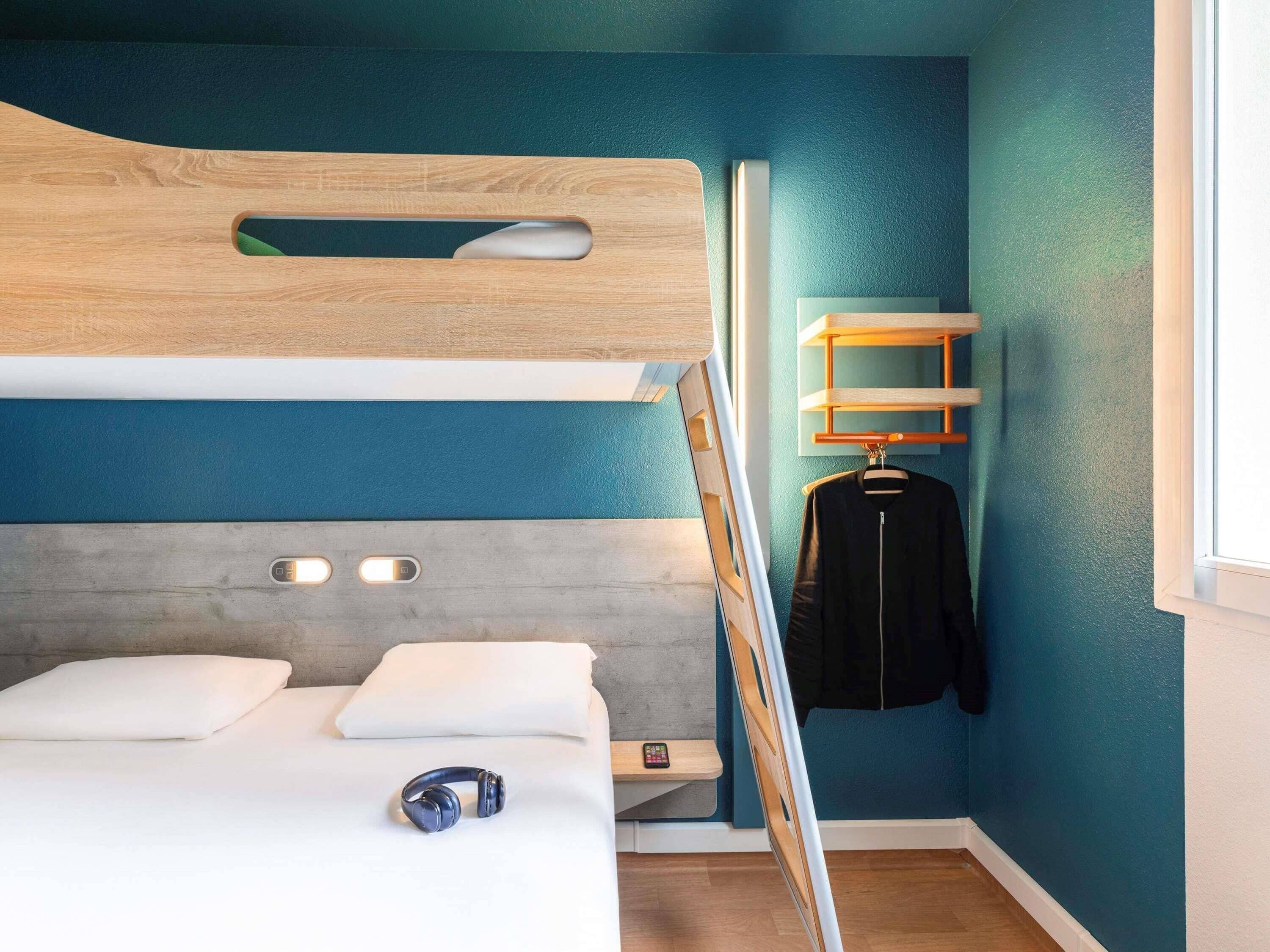 Uma cama de beliche com cabeceira de madeira, uma mesa de cabeceira com um controle remoto e um casaco pendurado.