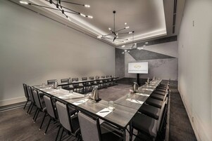 Uma sala de conferência com uma mesa grande, cadeiras, tela de projetor e um lustre moderno.
