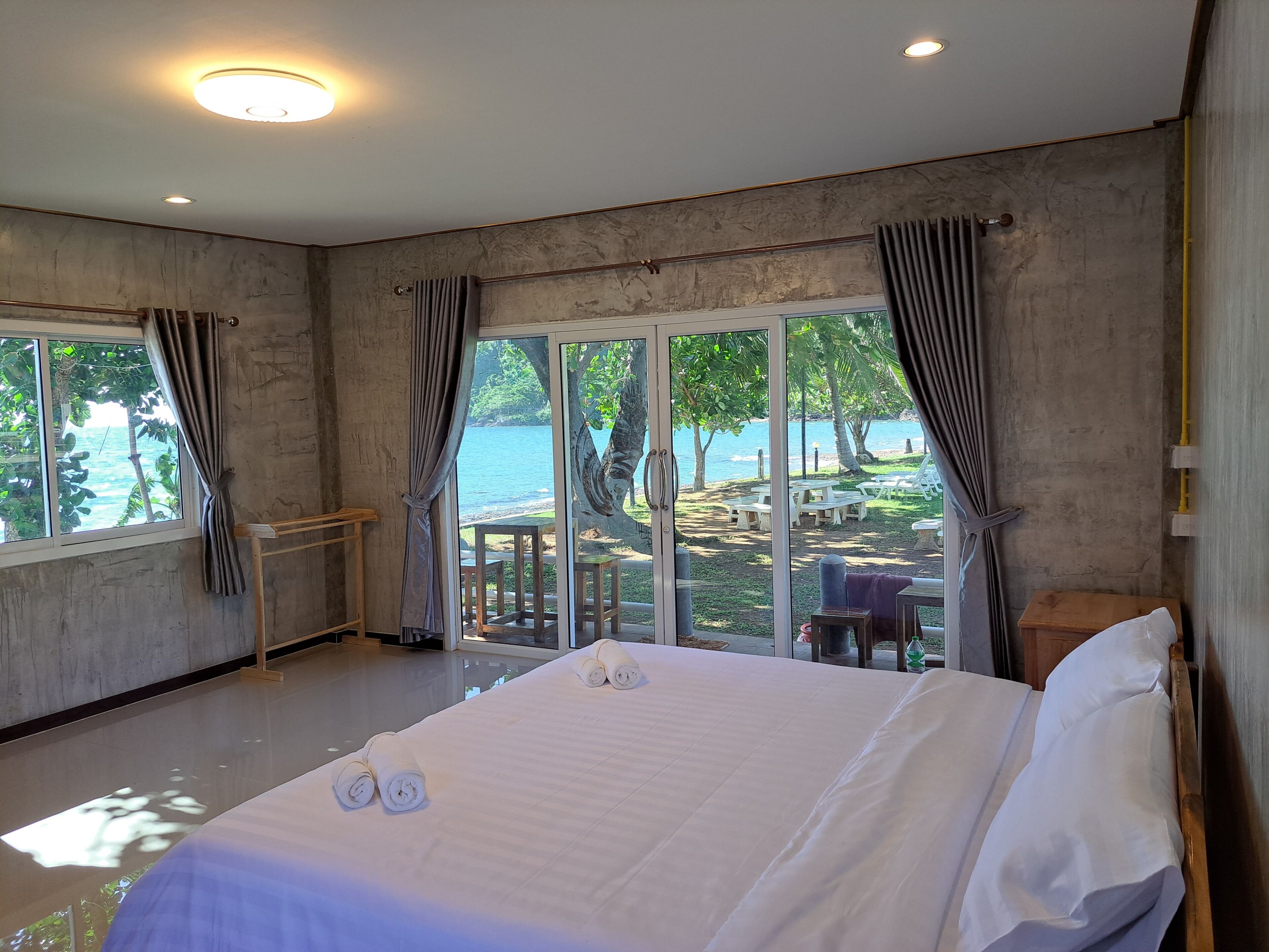 Quarto de hotel com uma cama grande, vista para o mar e varanda com mobiliário.