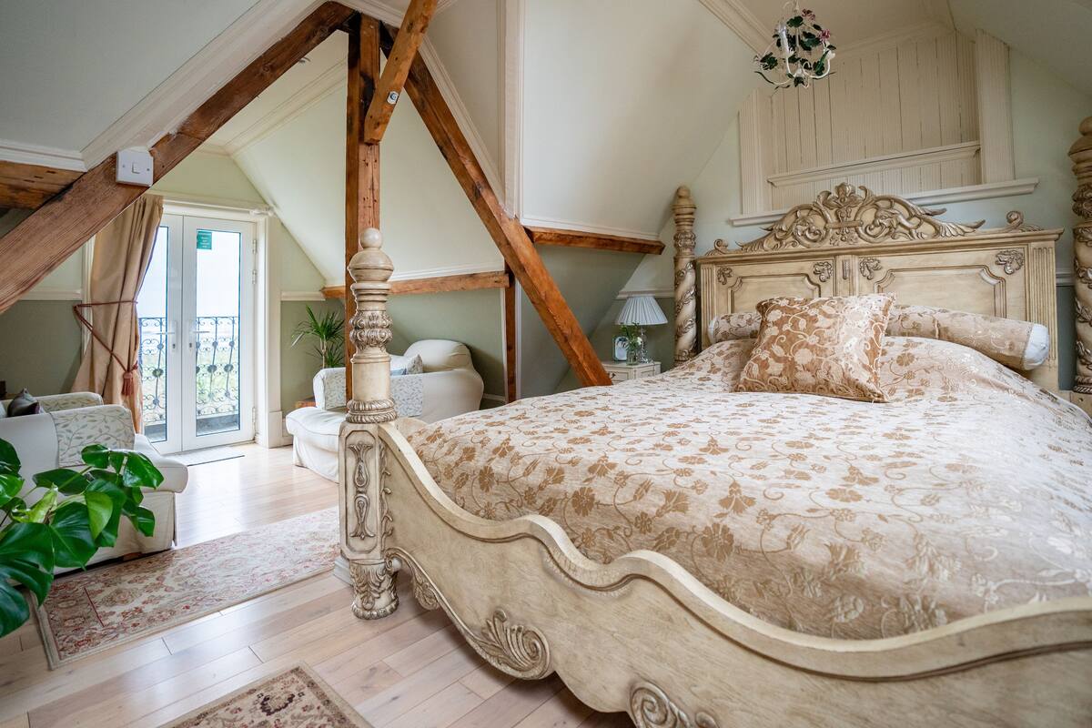 Quarto com uma cama grande, vigas de madeira, um candelabro e vista para o exterior.