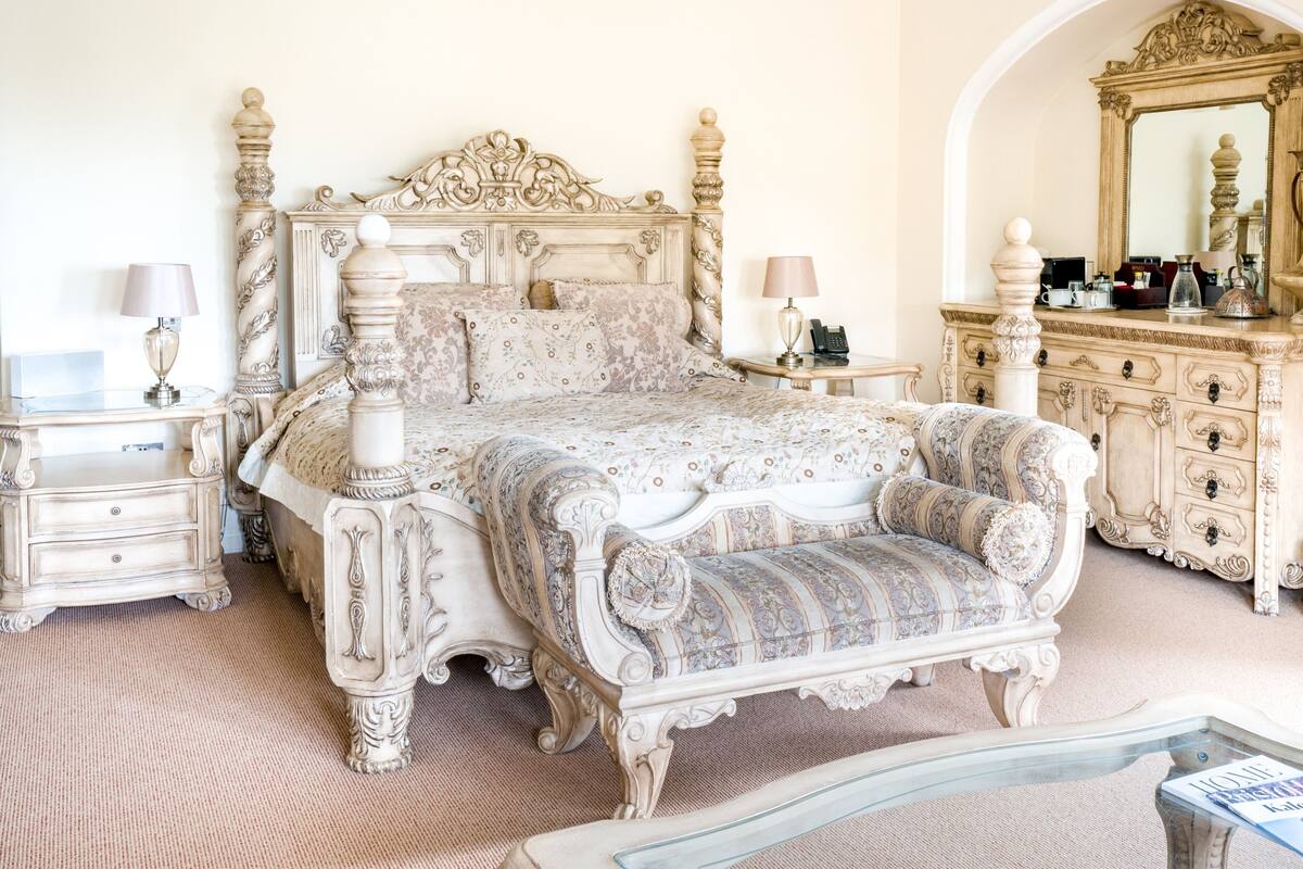 Quarto clássico e ricamente decorado, com uma cama grande, uma poltrona combinando e um penteado com espelho.