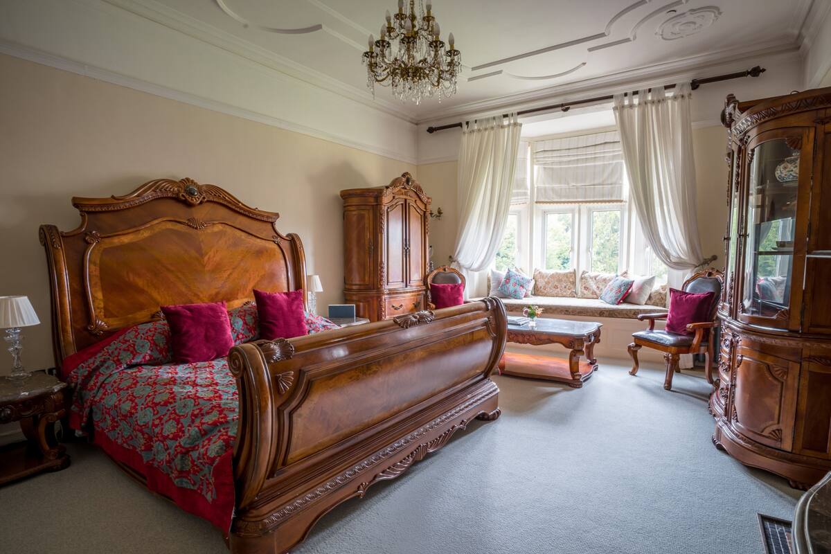 Um quarto amplo com uma cama de madeira grande, um aparador de madeira e uma janela com cortinas.