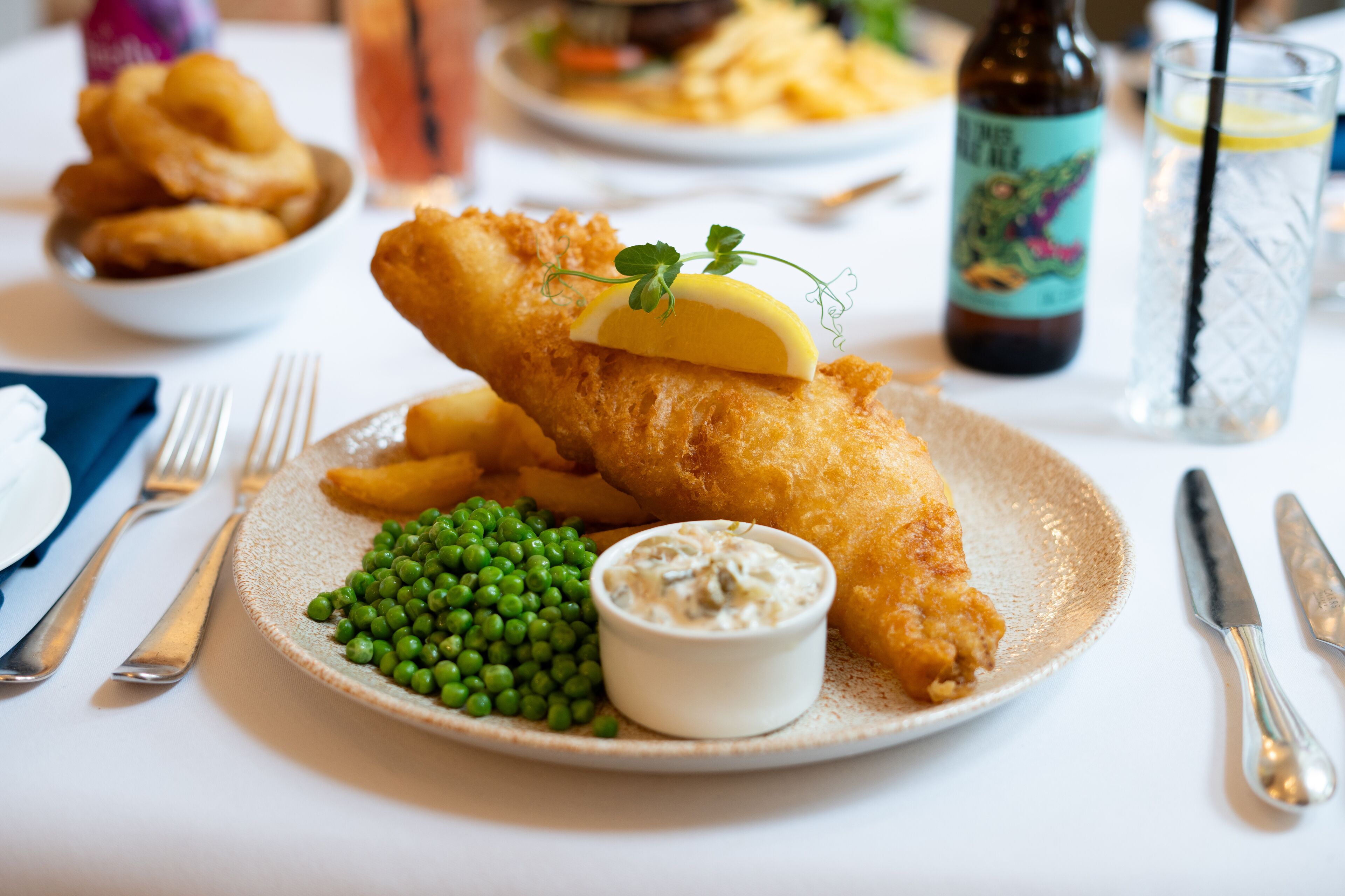 Prato de peixe com batatas fritas, ervilhas e molho para acompanhar.