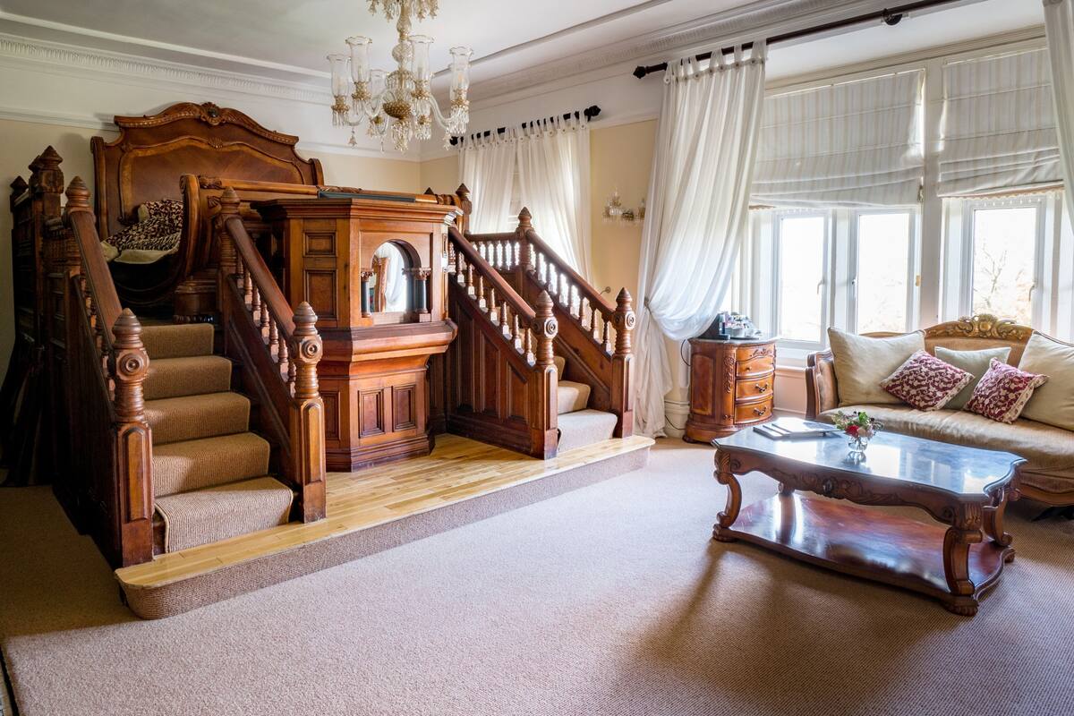 Uma escadaria imponente leva a um quarto, com um lustre grande e um sofá com almofadas.