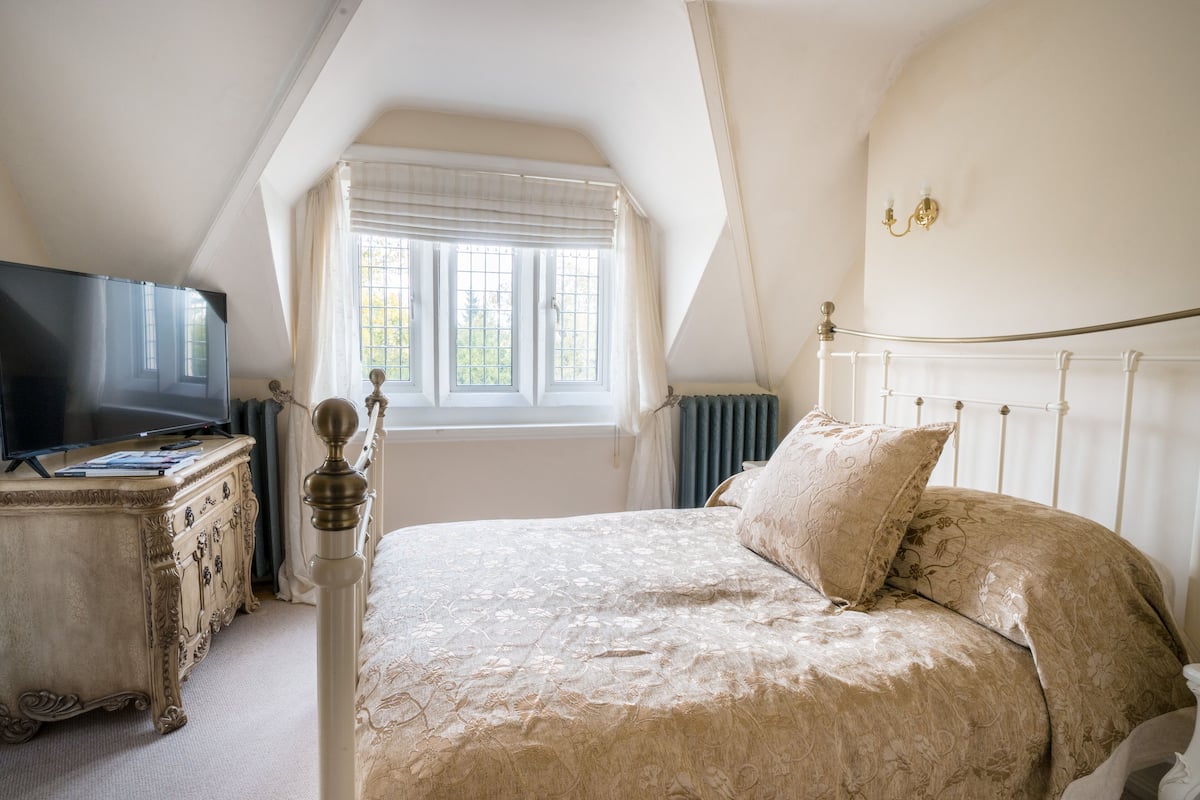 Quarto com uma cama grande, cômoda, televisão e janela com cortinas.