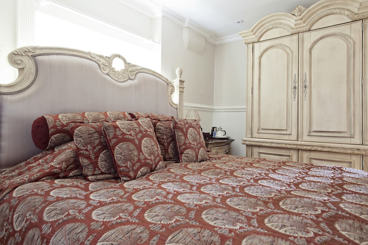 Quarto com uma cama grande, cabeceira elaborada e um guarda-roupa clássico.