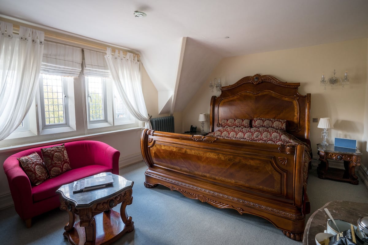 Quarto com uma cama de madeira grande, um sofá vermelho e uma mesa pequena.