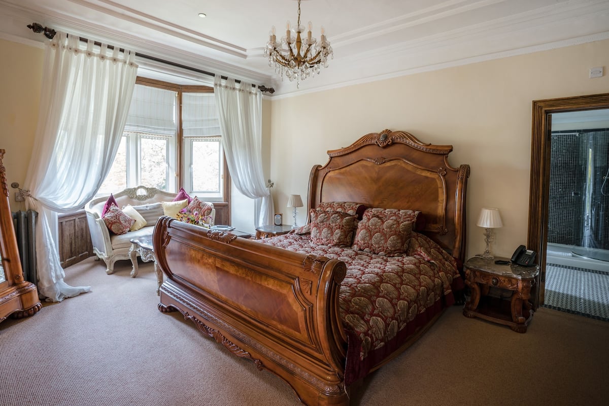 Um quarto espaçoso com uma cama de madeira grande, um candelabro e vista para um banheiro.