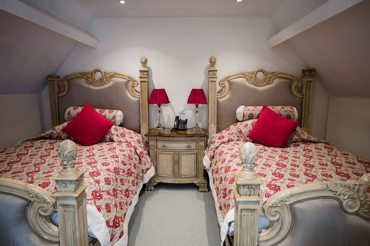 Quarto com duas camas, cada uma com cabeceiras elaboradas e almofadas vermelhas.