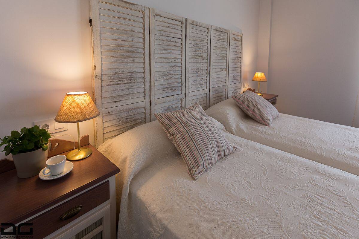 Quarto com duas camas, uma mesinha de cabeceira com abajur, um vaso de planta e uma xícara.