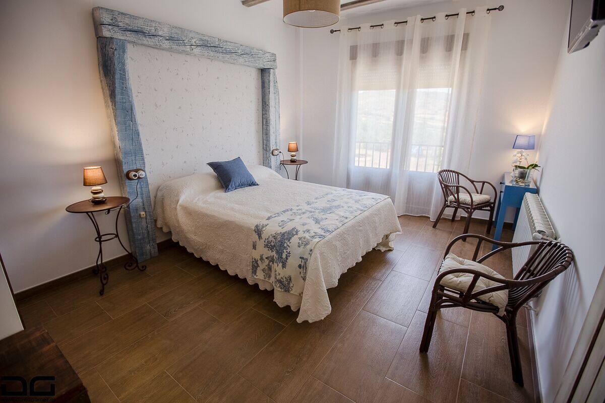 Quarto com cama grande, duas mesinhas de cabeceira, uma cadeira e janela com cortinas.