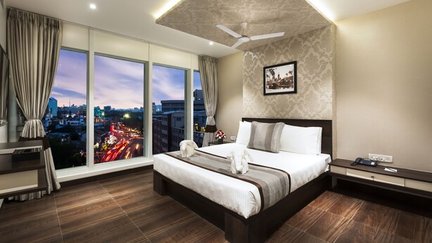 Quarto de hotel moderno com uma cama grande, uma escrivaninha e vista para a cidade ao entardecer.