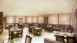 Um restaurante espaçoso com várias mesas e cadeiras, painéis de madeira nas paredes e teto com padrão de tijolos.