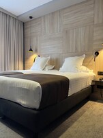 Quarto moderno com uma cama grande, painel de parede de madeira, duas luminárias de cabeceira e um telefone na mesa de apoio.