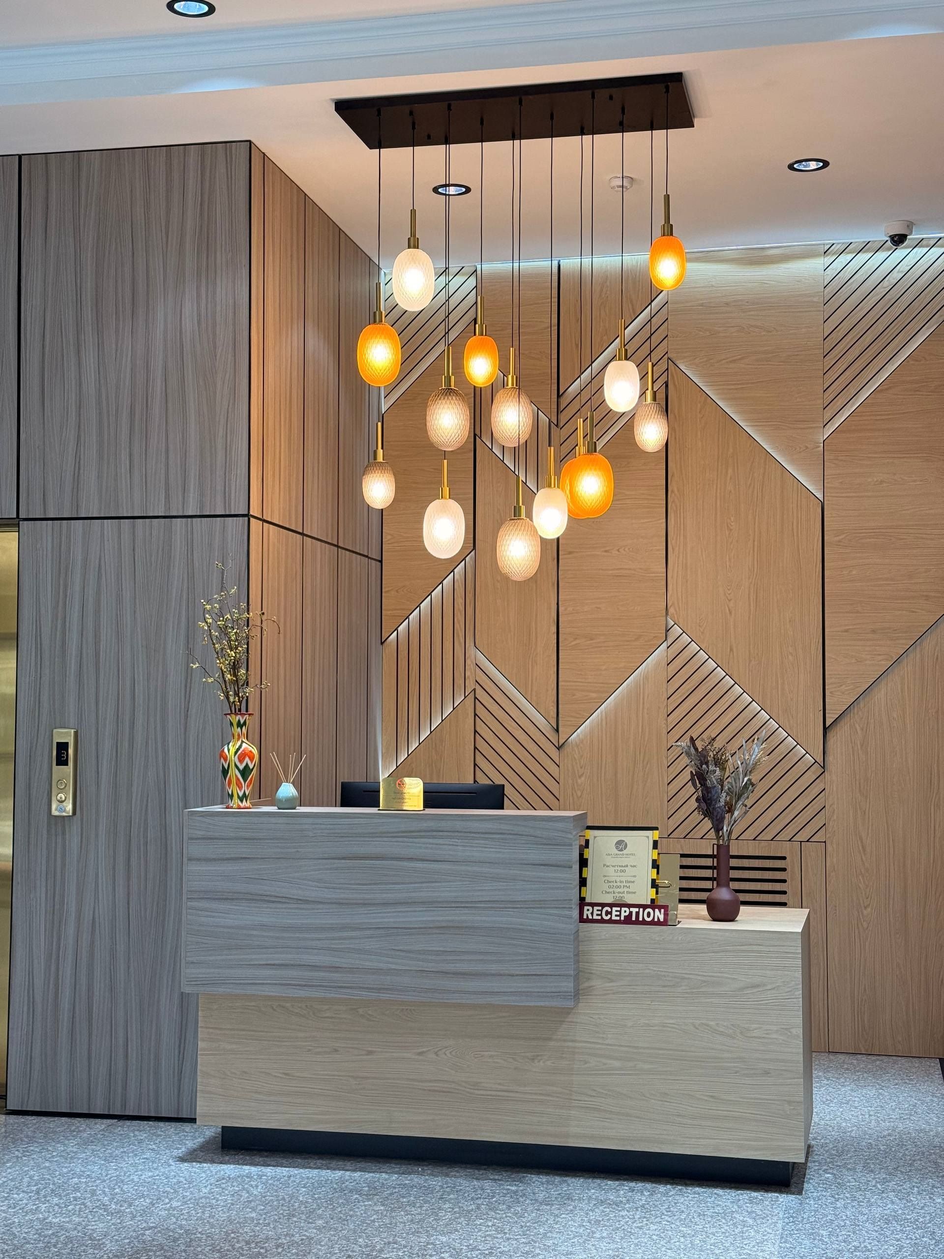 Balcão de recepção com design moderno, destacando um padrão geométrico na parede e uma série de luminárias esféricas suspensas.