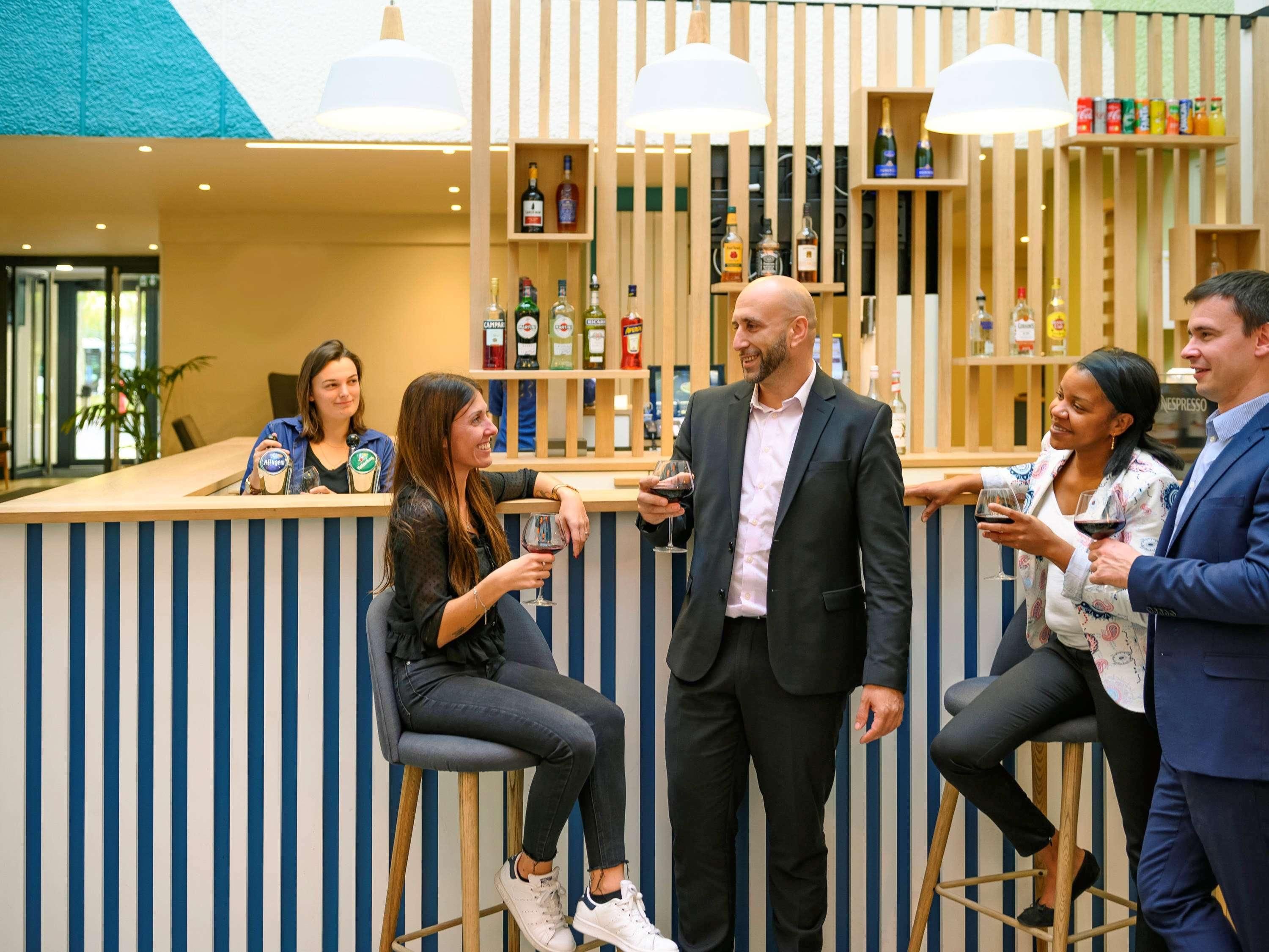 Uma área de bar com balcão e banquetas, prateleiras com garrafas e uma parede de ripas de madeira.
