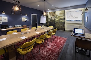 Uma sala de conferências com uma mesa comprida, cadeiras amarelas, um tapete vermelho e uma tela grande exibindo um gráfico.