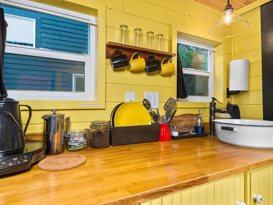 Cozinha com bancadas de madeira, cafeteira, pia e diversos utensílios.