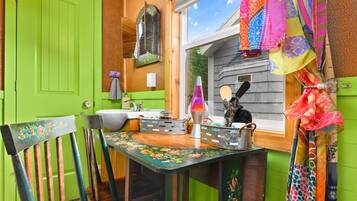 Uma cozinha pequena e vibrante, com uma porta verde, uma janela com vista e uma mesa com toalha de mesa florida.