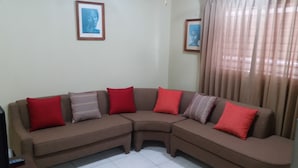 Um sofá modular em formato de L com almofadas vermelhas e listradas, um controle remoto no chão e duas fotos emolduradas na parede.
