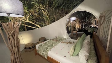 Um quarto em formato de tenda circular, com uma cama, um abajur e um banquinho pequeno.