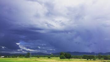 Paisagem rural com campos, árvores e montanhas distantes sob um céu nublado.