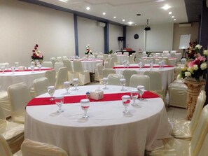 Sala de conferência com várias mesas redondas, cada uma com toalhas brancas e jogos americanos vermelhos.