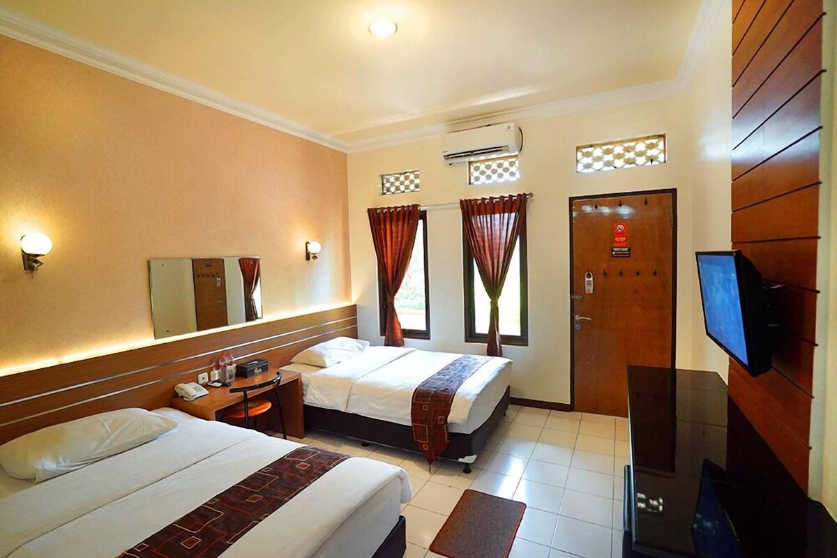 Quarto de hotel com duas camas, uma escrivaninha, uma cadeira, uma televisão e um aparelho de ar condicionado.
