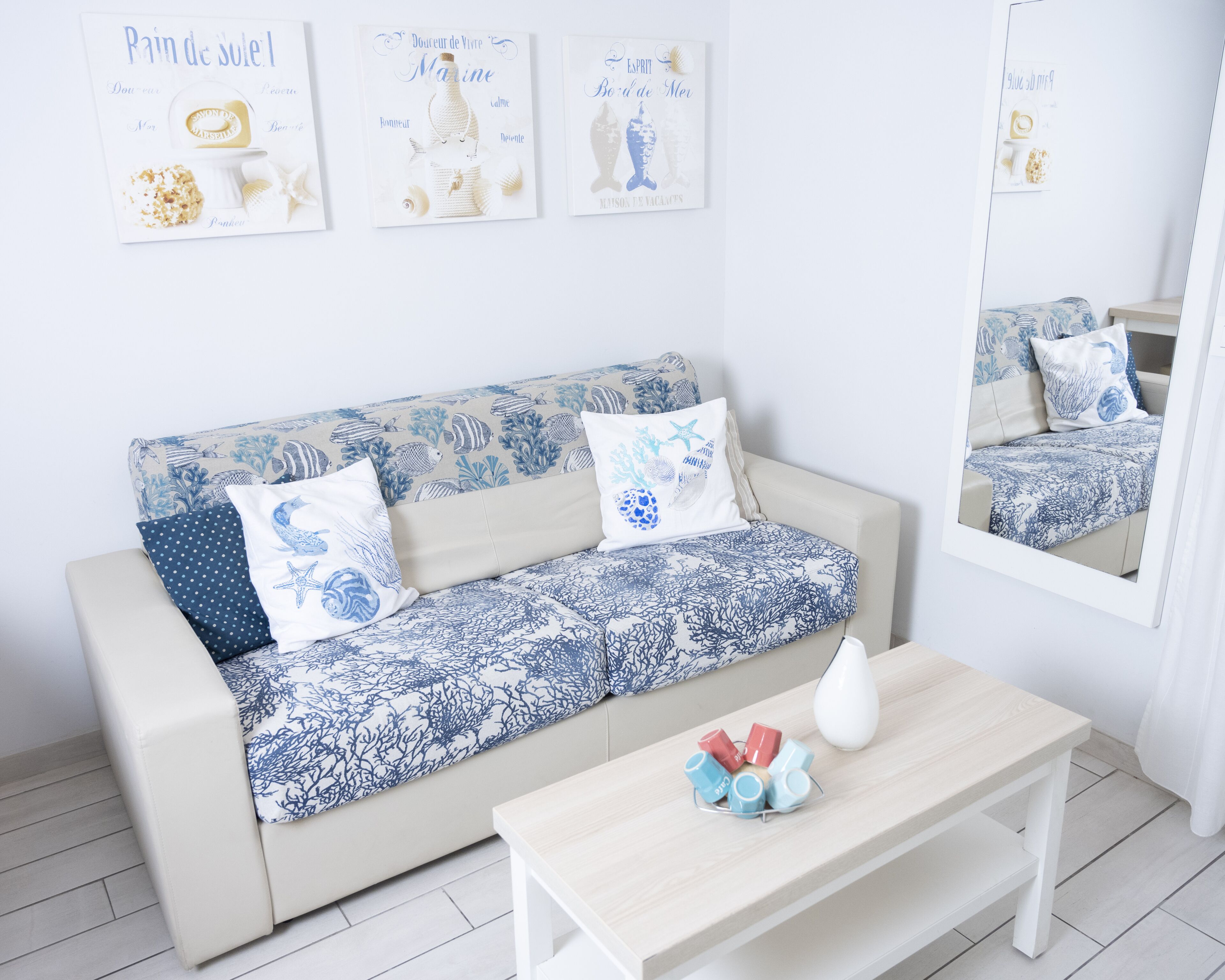 Uma sala de estar moderna com um sofá apresentando um padrão azul e branco inspirado no oceano, uma mesa de centro com objetos decorativos e arte na parede retratando vida marinha.