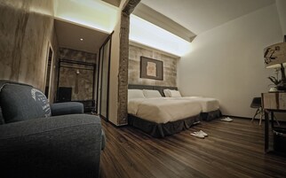 Quarto de hotel com uma cama, uma cadeira, uma escrivaninha com abajur e um quadro pendurado na parede.