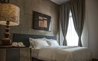 Quarto de hotel com uma cama grande, uma mesa de cabeceira, um abajur e um quadro na parede.