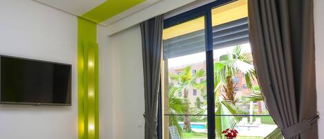 Quarto de hotel com cama, televisão fixada na parede, janela com cortinas e vista para o exterior.