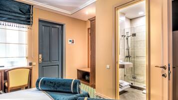 Quarto de hotel com cama, escrivaninha, cadeira, guarda-roupa e banheiro com chuveiro e vaso sanitário.